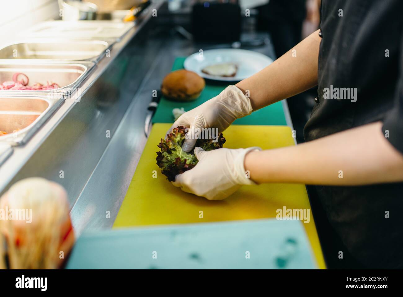 Male cook prepares fresh salad for burger. Hamburger preparation ...