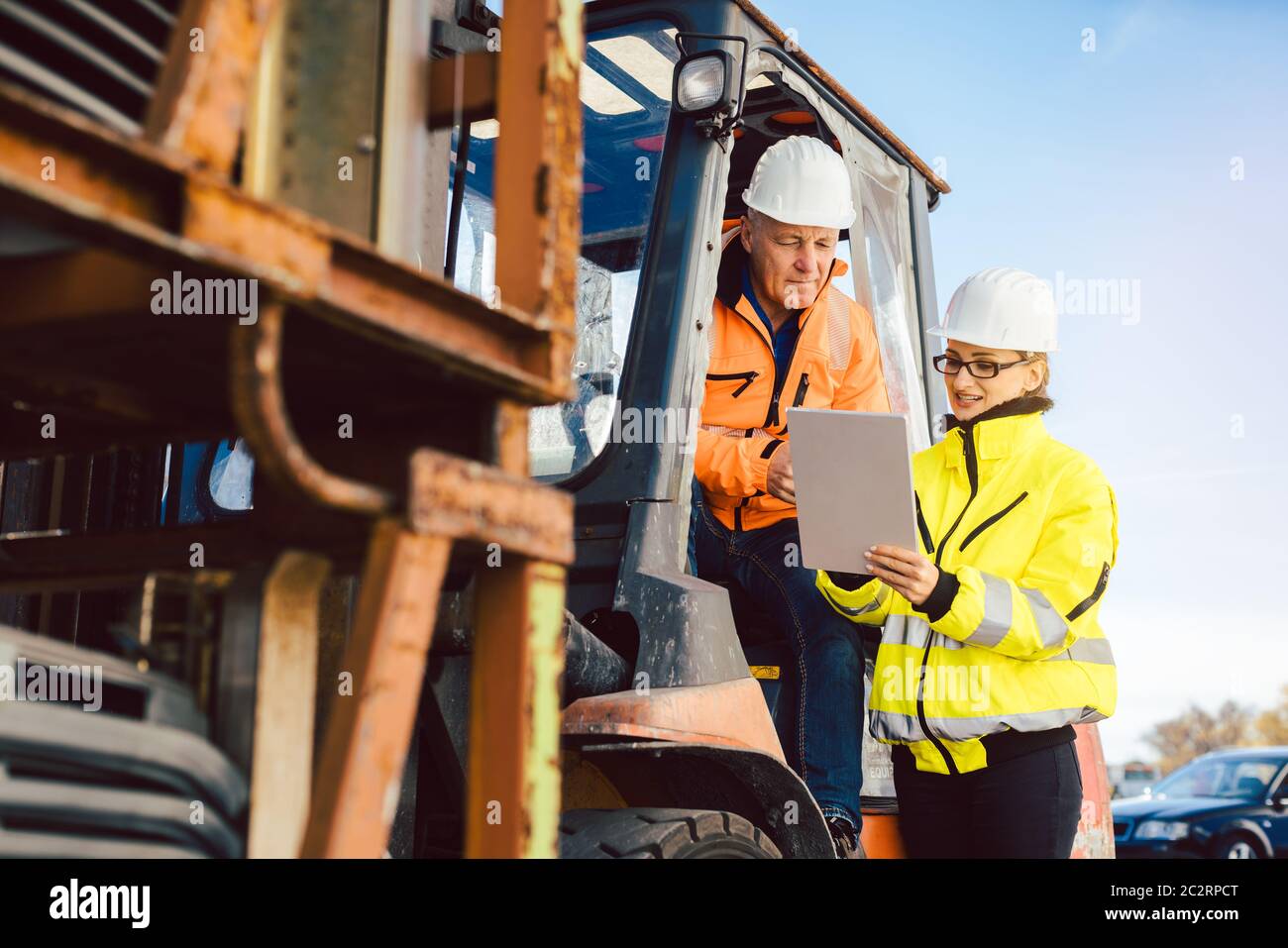 Worker in forklift and forewomen looking into task list on a tablet ...