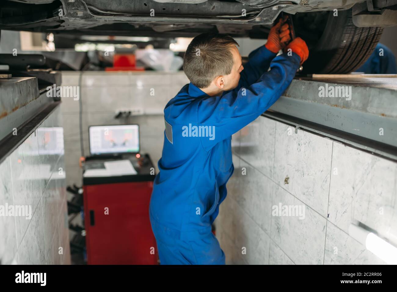 Mechanic adjusts the wheel angles on stand in auto-service. Computer ...
