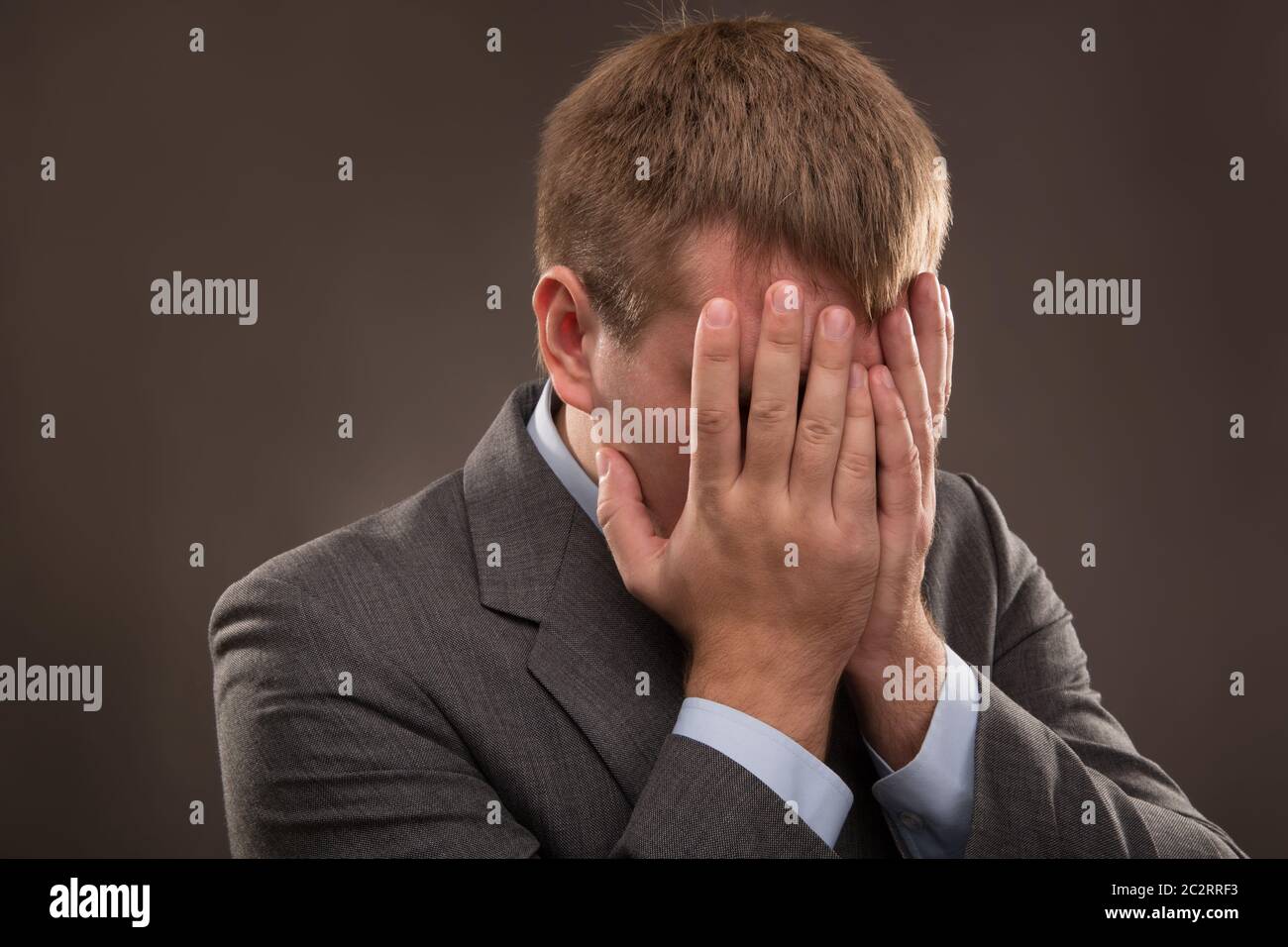 Young man in a suit covered his face with his hands Stock Photo - Alamy