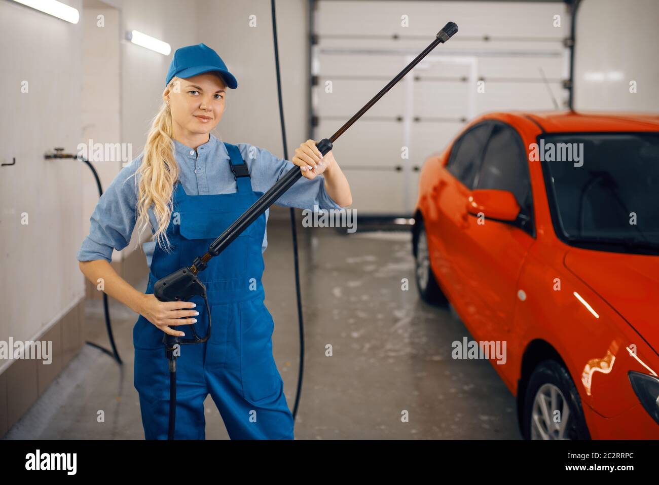 Female washer in uniform poses with high pressure gun in hands, car ...