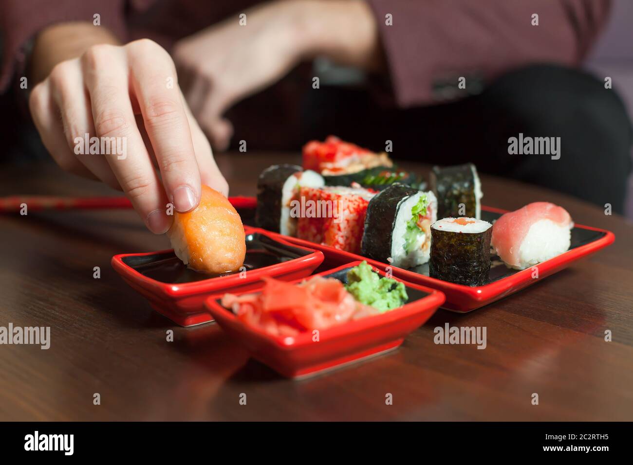 Man eats sushi roll with hands. Japanese seafood on wooden table. Sushi ...