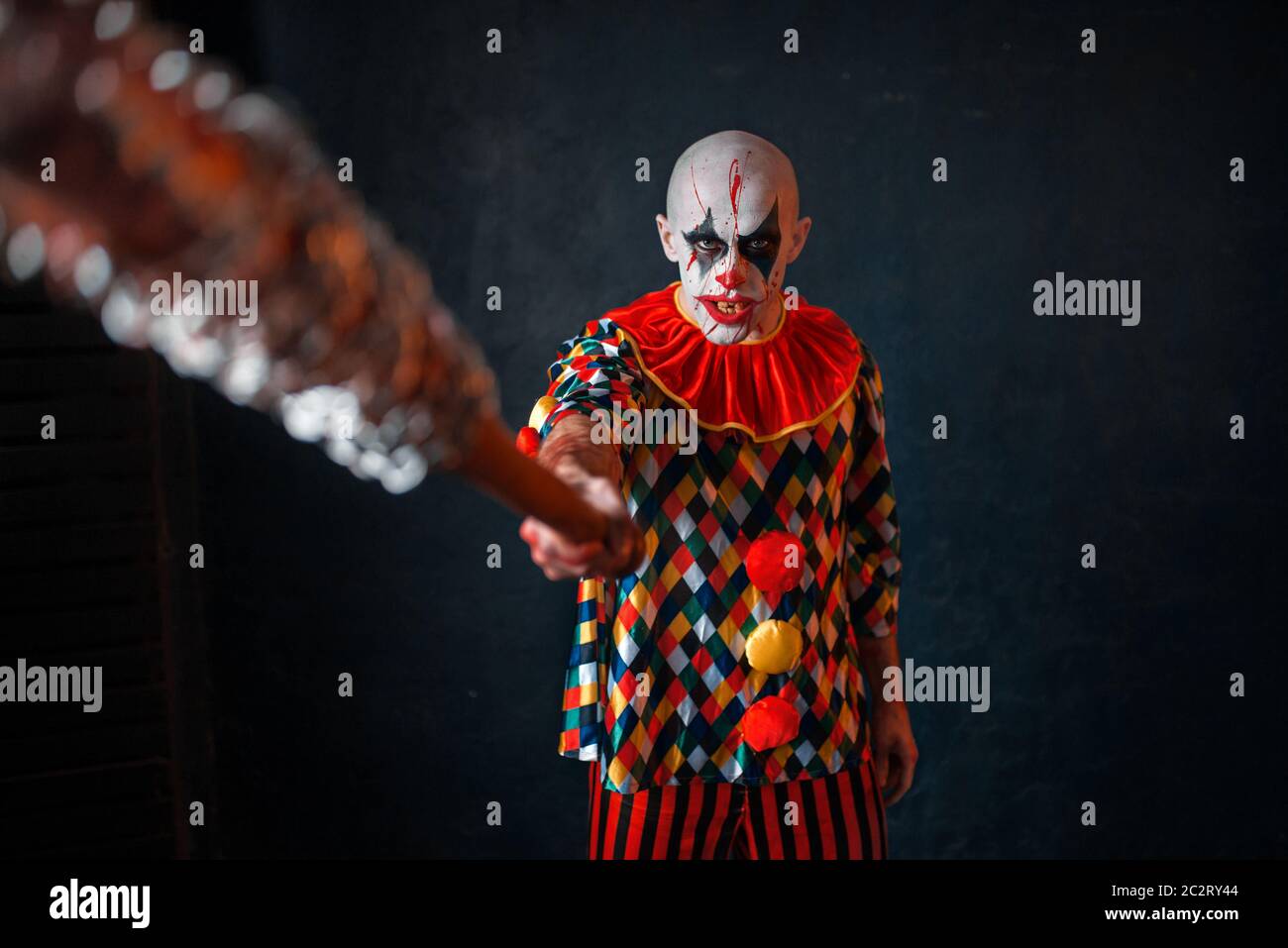 Scary bloody clown reaches out baseball bat. Man with makeup in ...