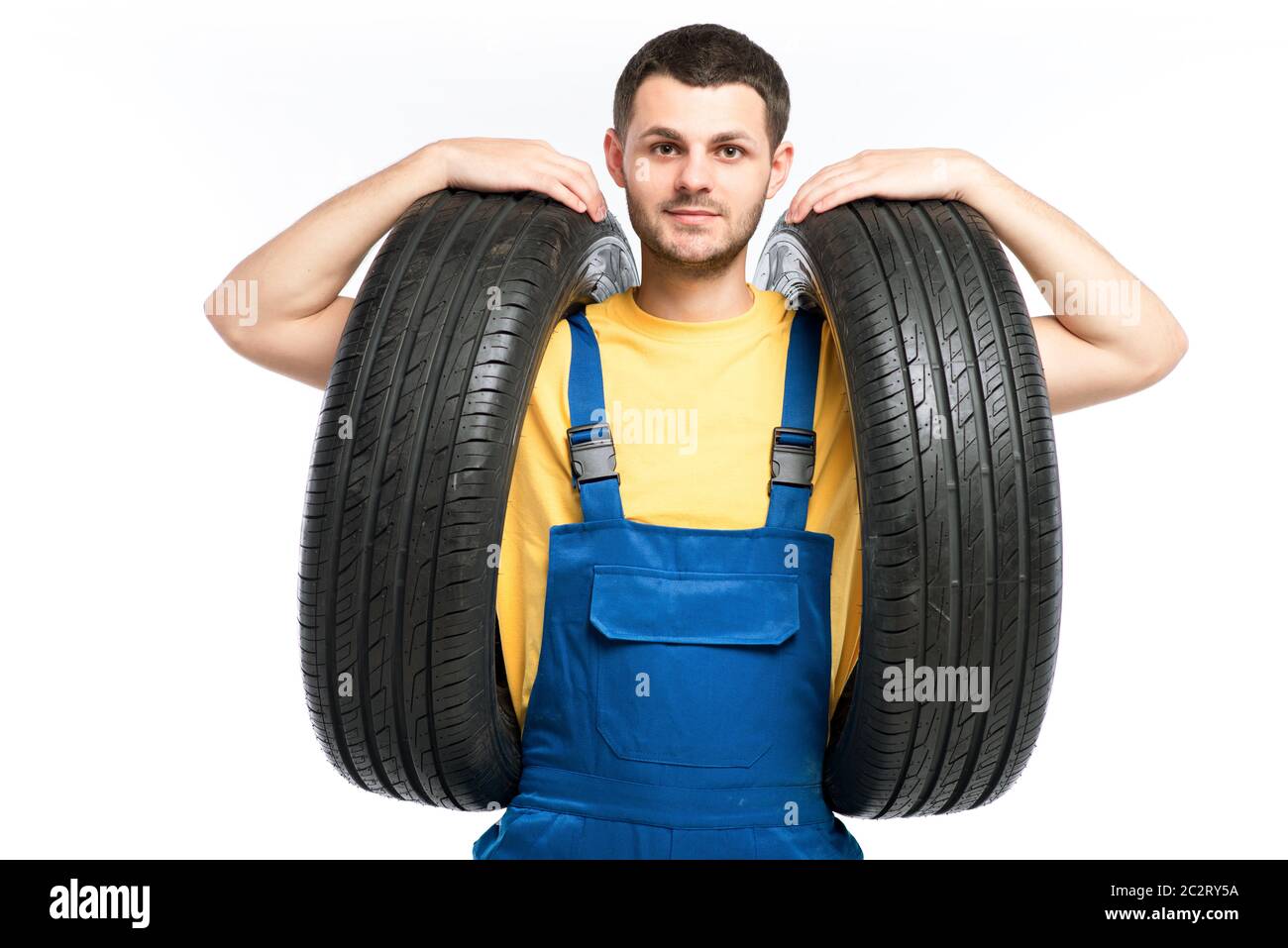 Tire service worker in blue uniform holds car tyres in hands, white ...
