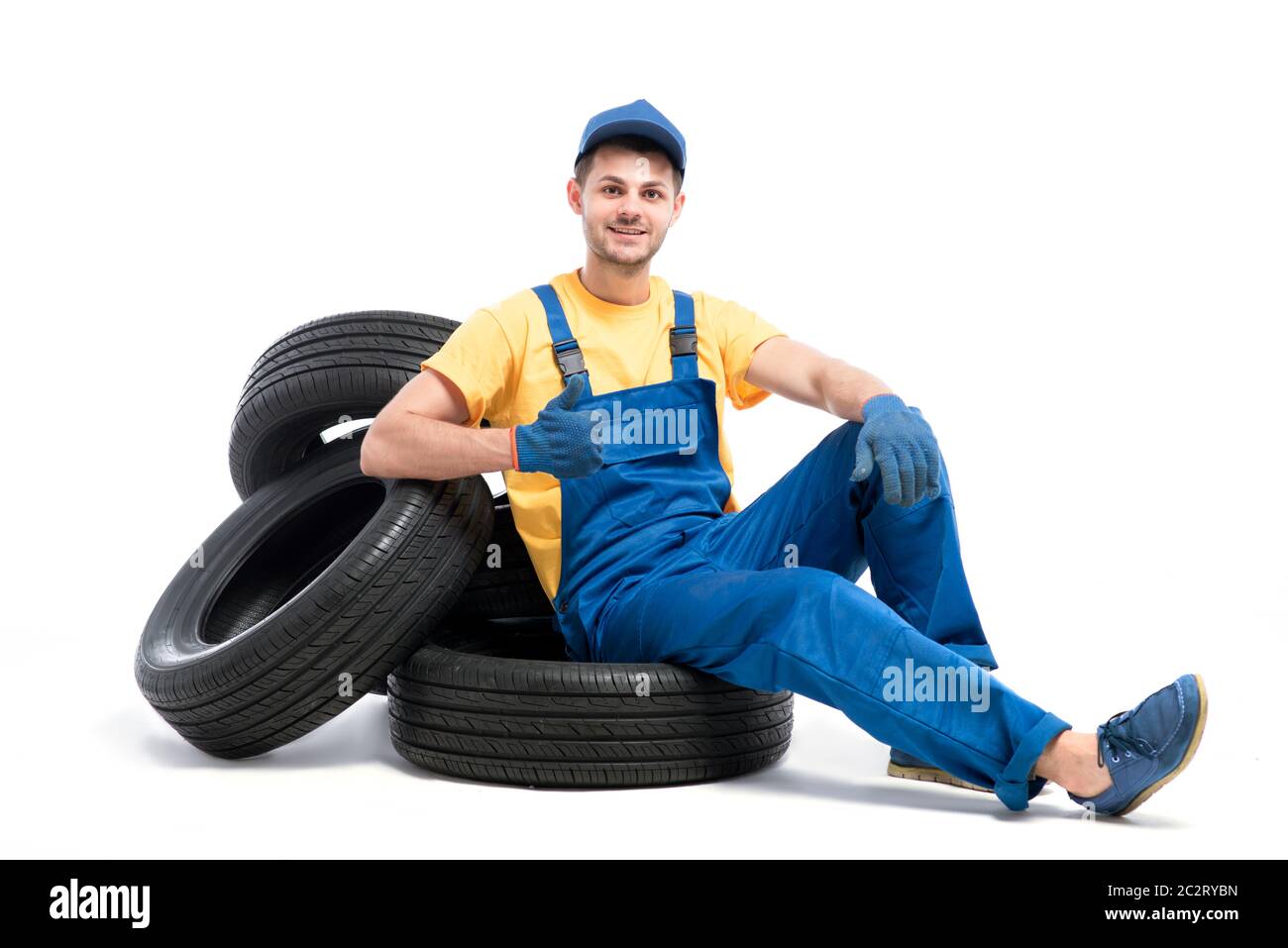 Service worker in blue uniform sitting on car tires, white background ...