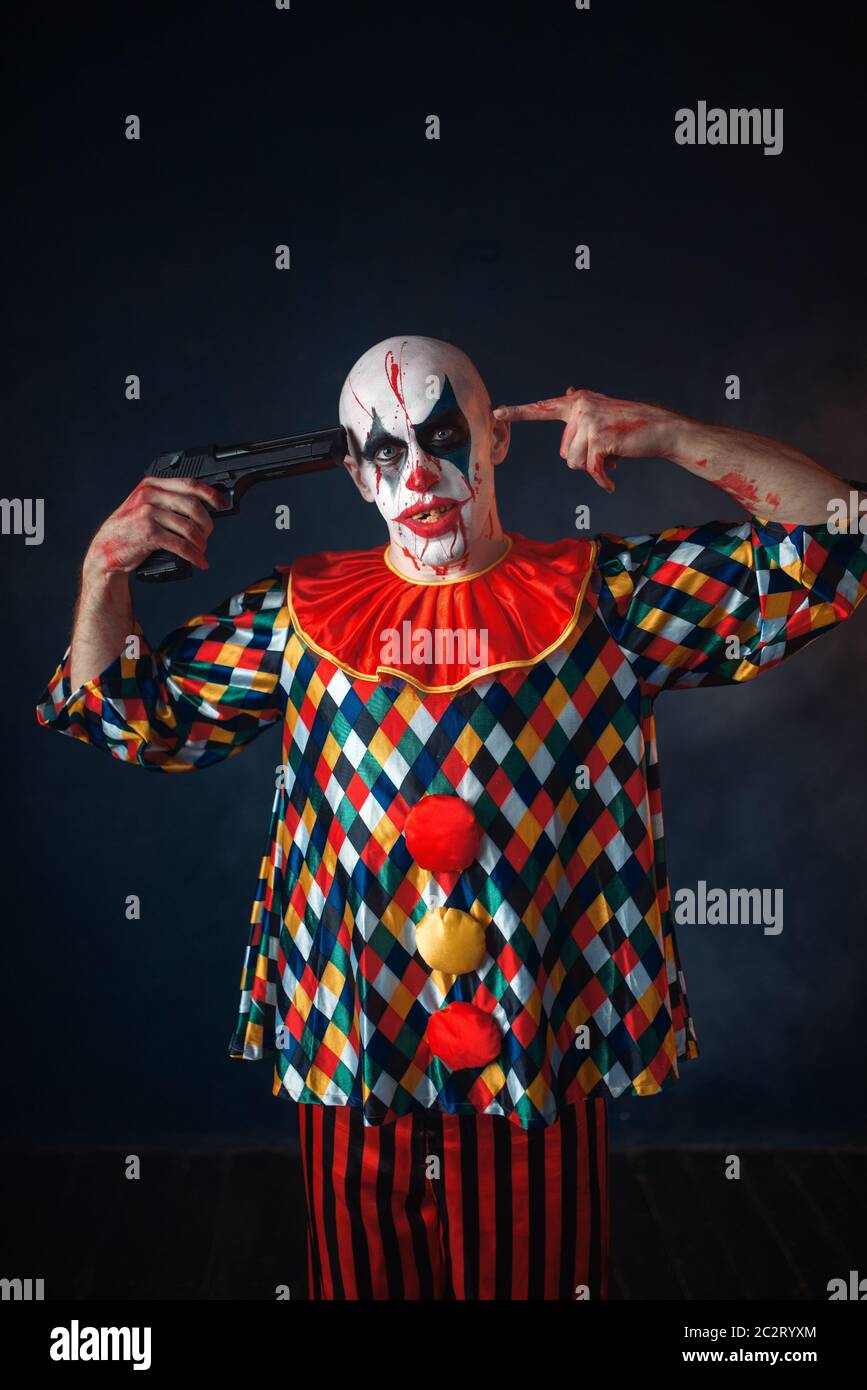 Mad bloody clown with a gun in his head, circus horror. Man with makeup ...