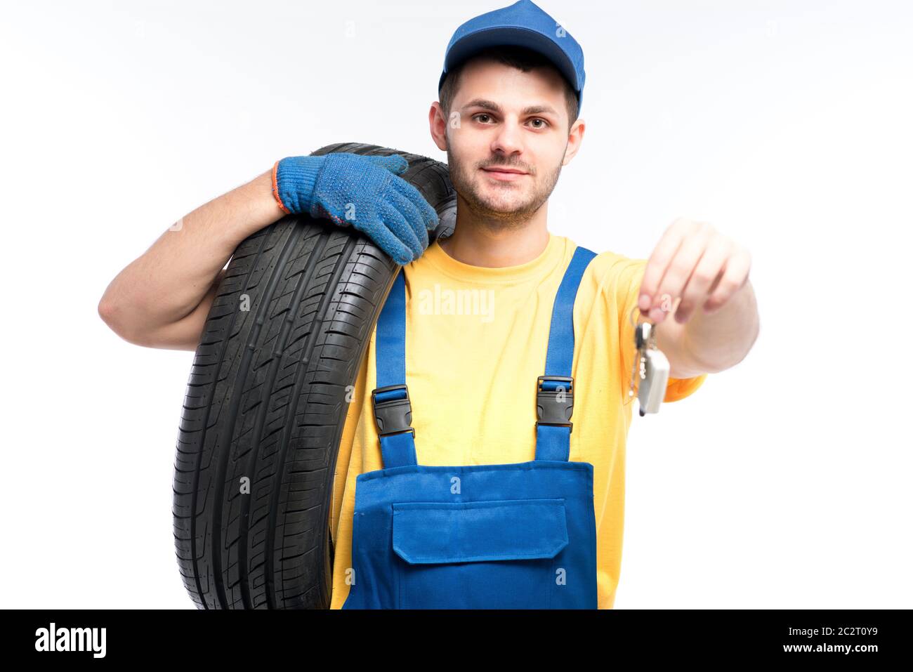 Tyre service, worker in blue uniform holds tire and car keys in hands ...