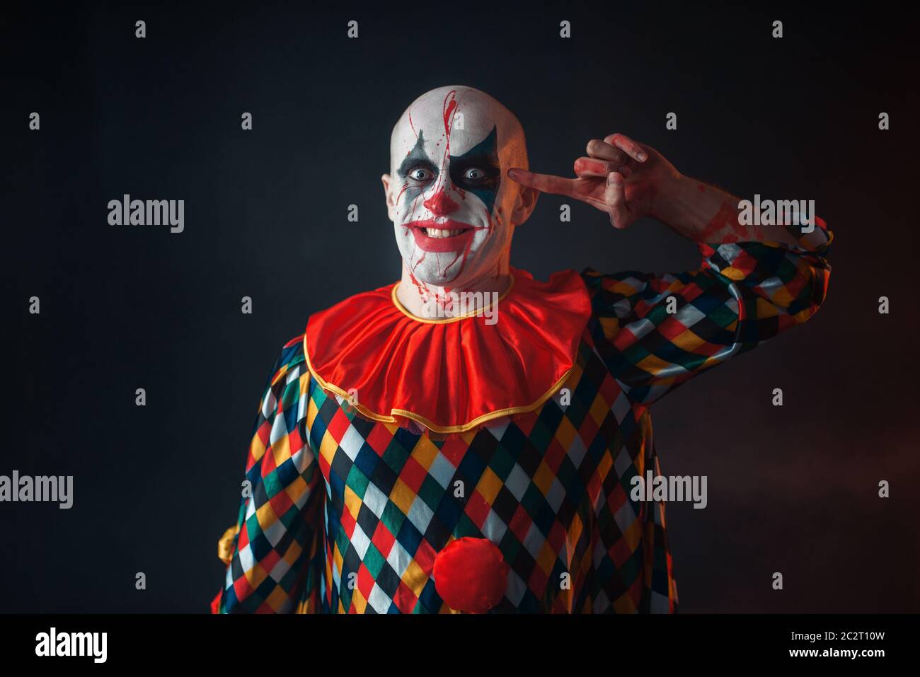Portrait of mad bloody clown twirls finger to his temple, face in blood ...