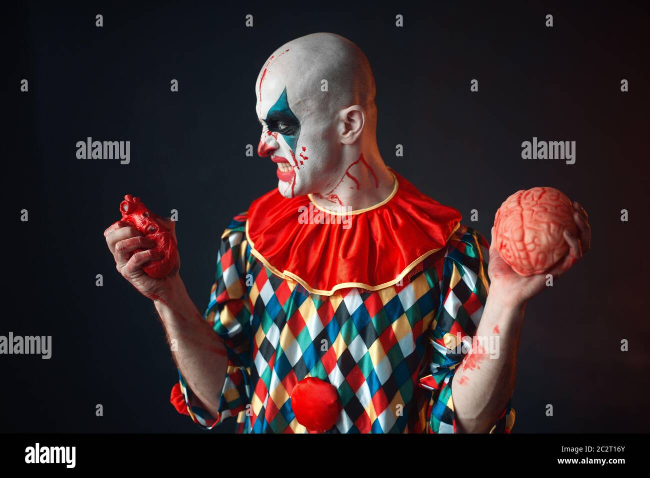 Mad bloody clown holds human heart and brain. Man with makeup in ...