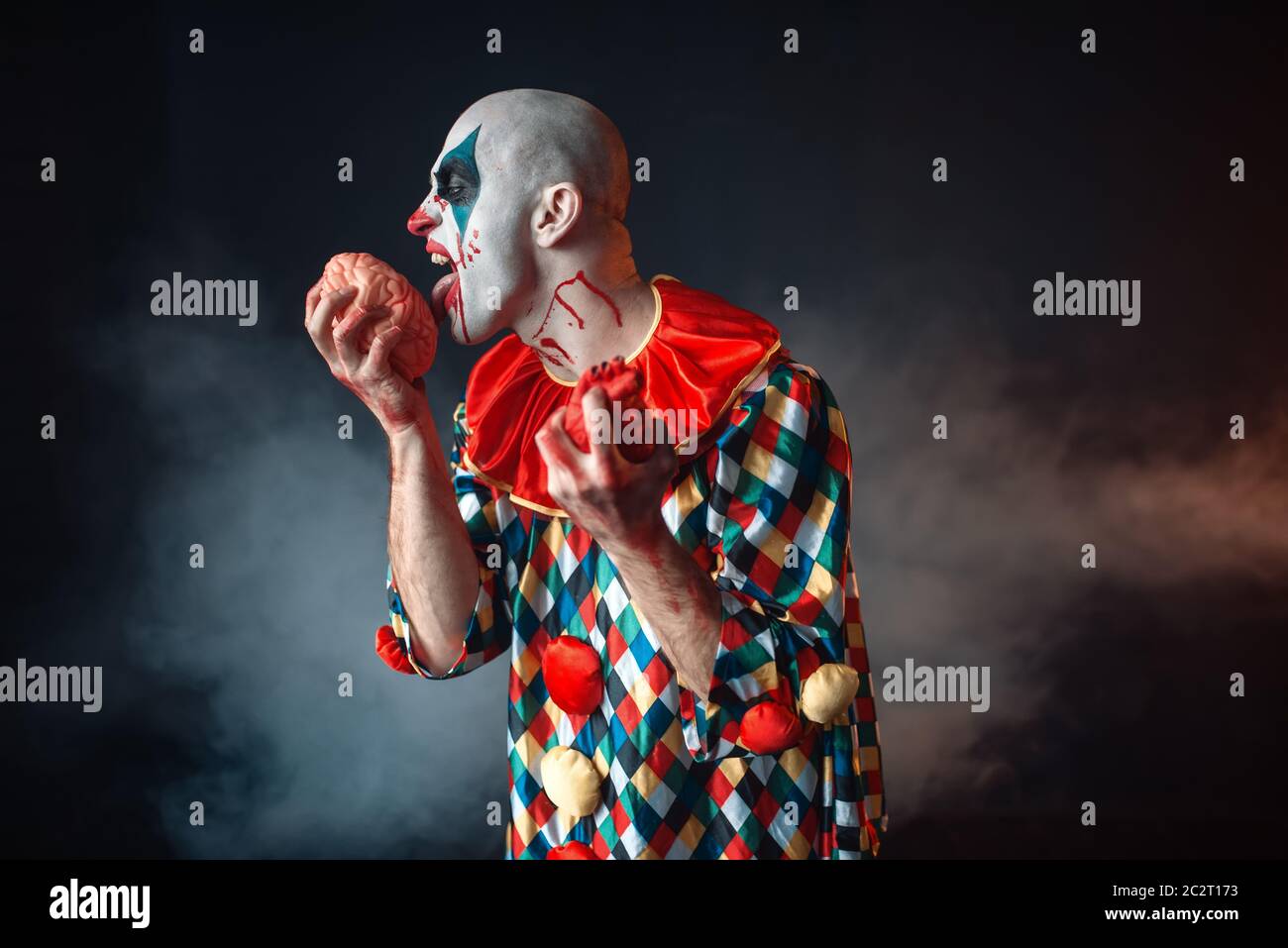 Mad bloody clown licks human brain. Man with makeup in carnival costume ...
