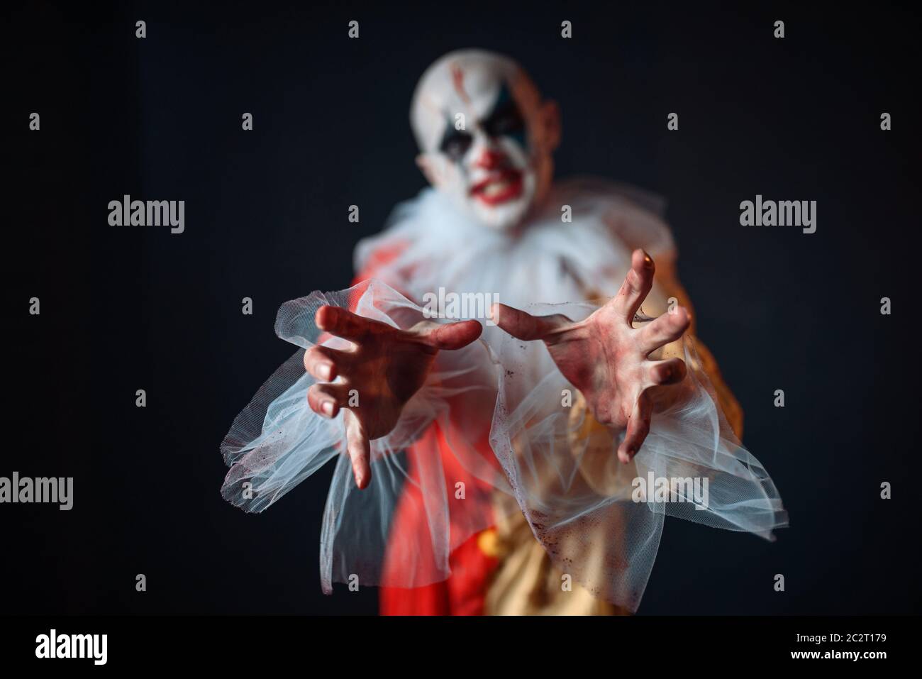 Mad bloody clown reaching for the victim with his hands, front view ...