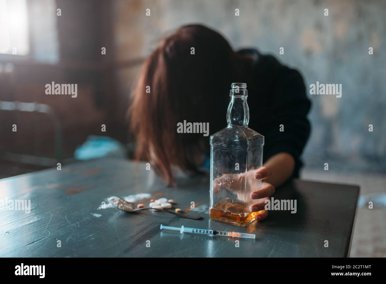 Female junkie with bottle of alcohol sitting at the table with drugs ...