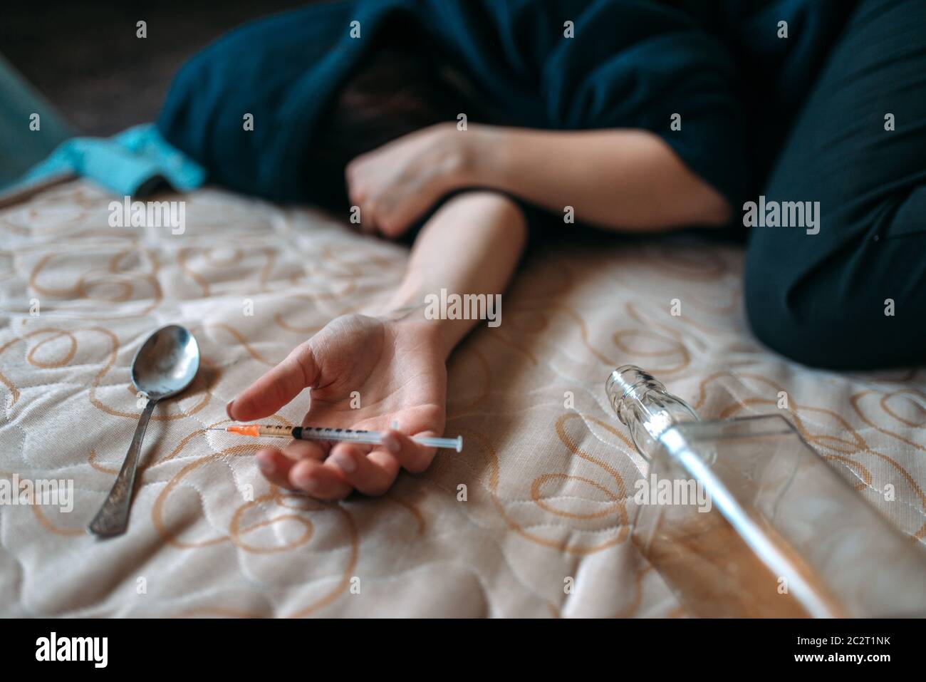 Female druggy with syringe in hand lies in bed, bottle of alcohol and ...