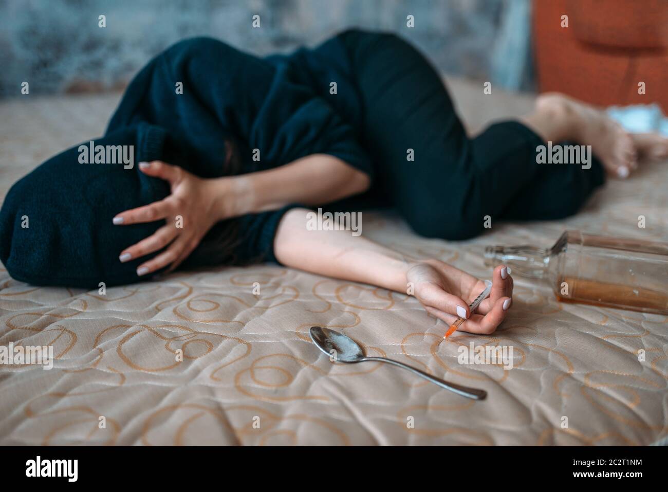 Female druggy with syringe in hand lies in bed, bottle of alcohol and ...