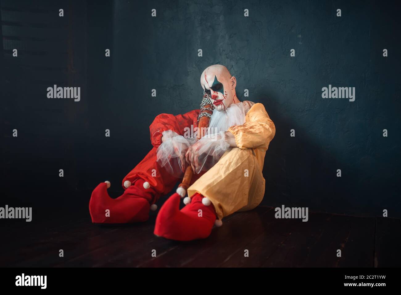 Tired bloody clown with baseball bat sitting on the floor. Man with ...