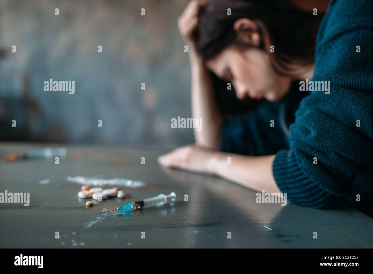 Female drug addict sitting at the table with narcotics and syringe ...