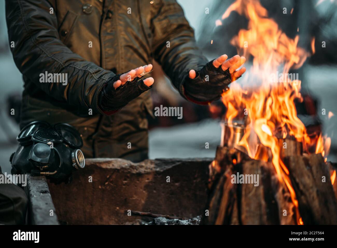 Stalker, male person warms his hands on fire. Post apocalyptic ...