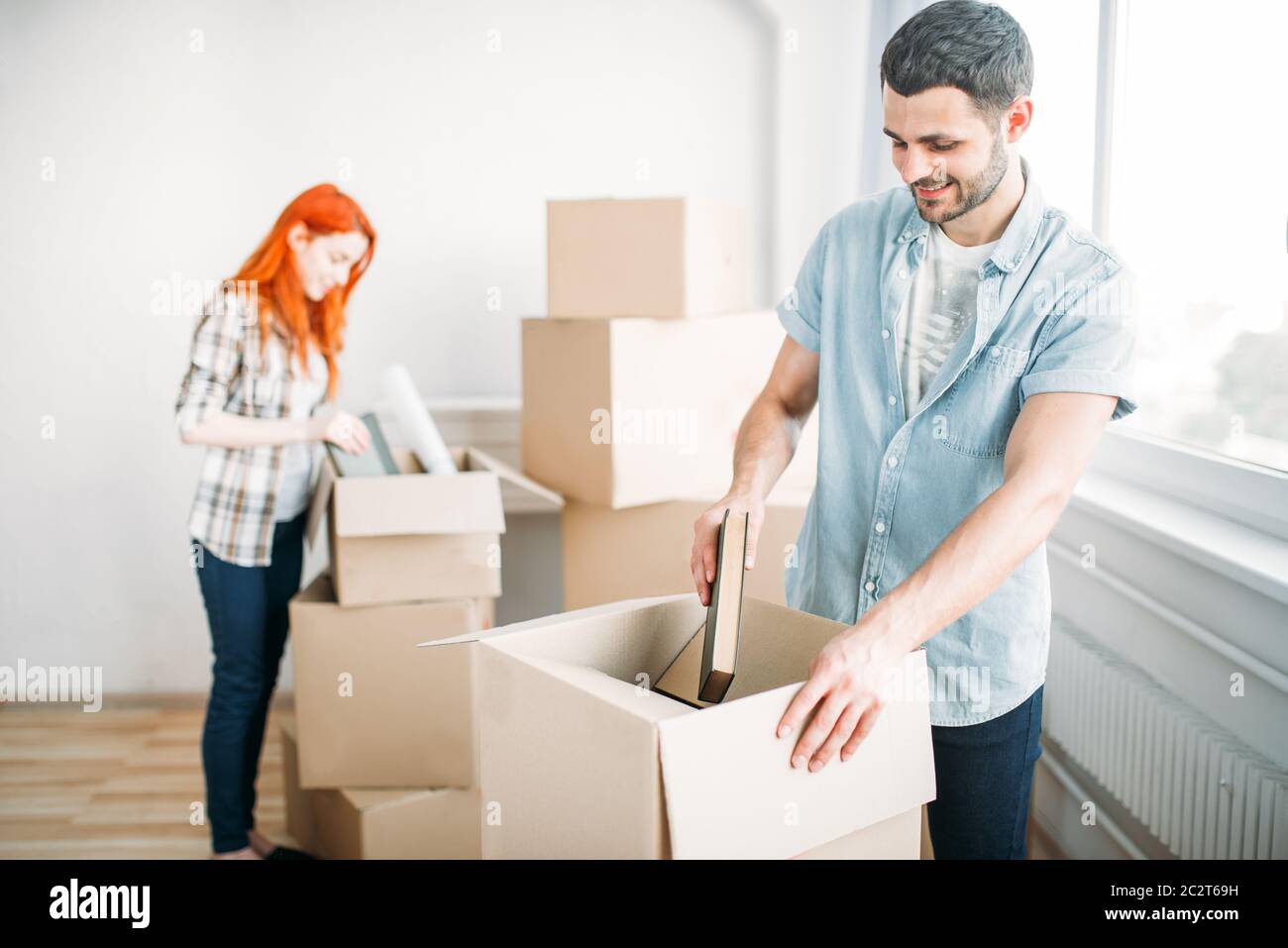 Young man unpacking cardboard boxes with books, housewarming. Moving to ...