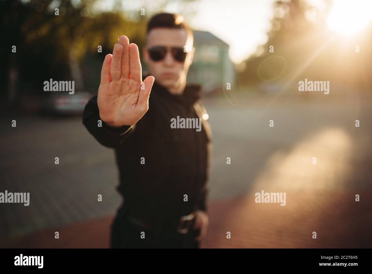 Serious police officer in uniform and sunglasses shows a hand stop sign ...