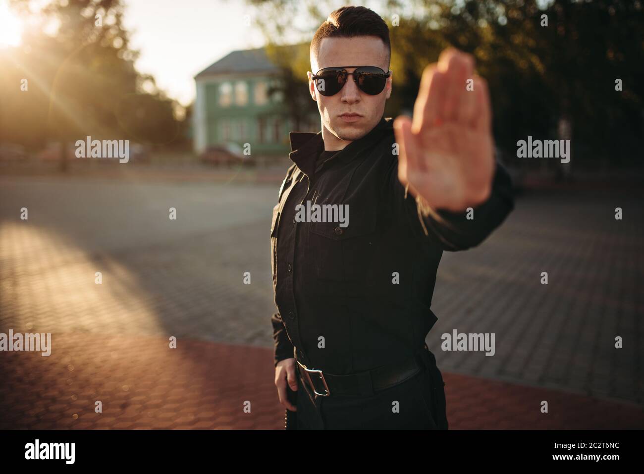 Serious police officer in uniform and sunglasses shows a hand stop sign ...
