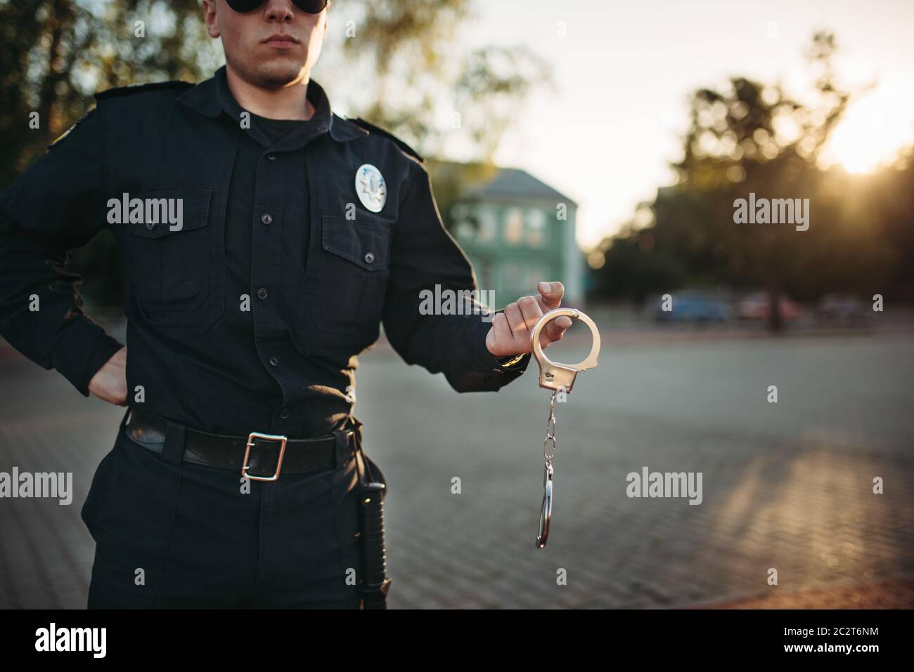 Serious police officer in uniform and sunglasses holds hand handcuffs ...