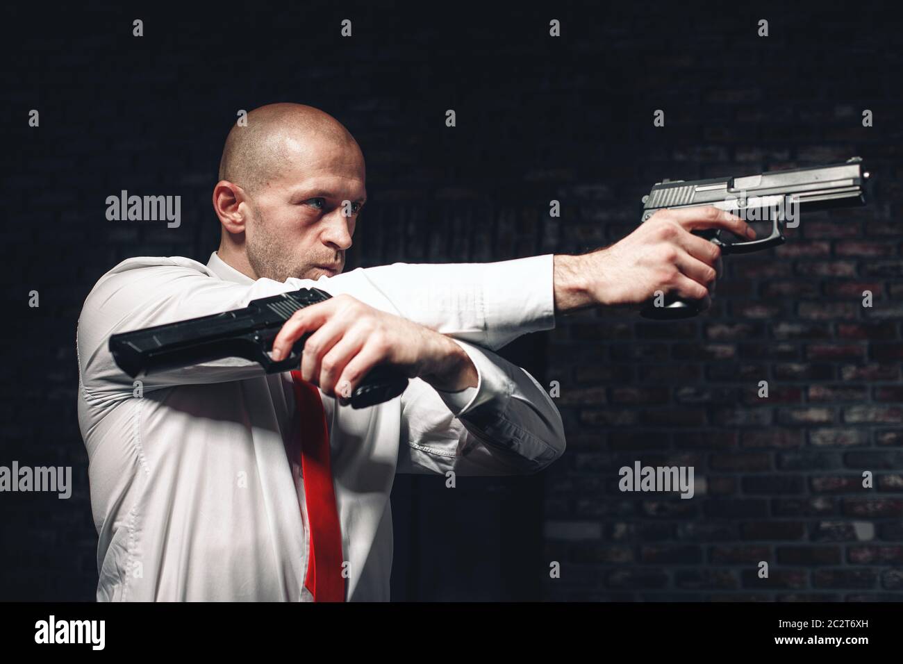 Serious hired assasin in red tie aims with two pistols. Professional ...