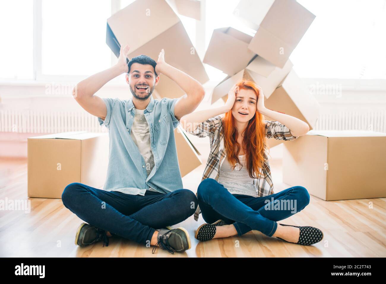 Playful couple sitting on the floor in yoga pose among carton boxes ...
