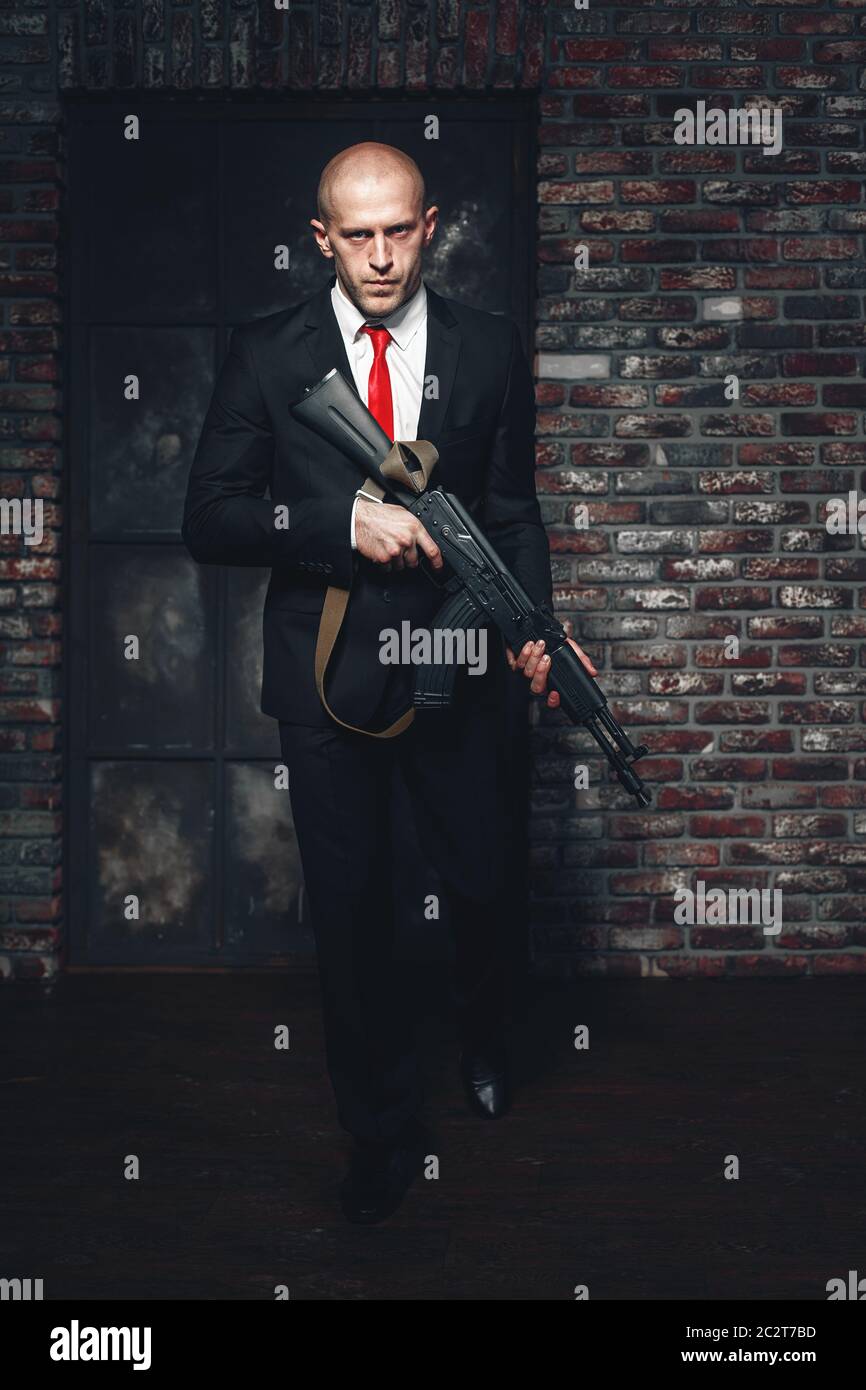 Assassin in suit and red tie holding machine gun in hands. Contract ...