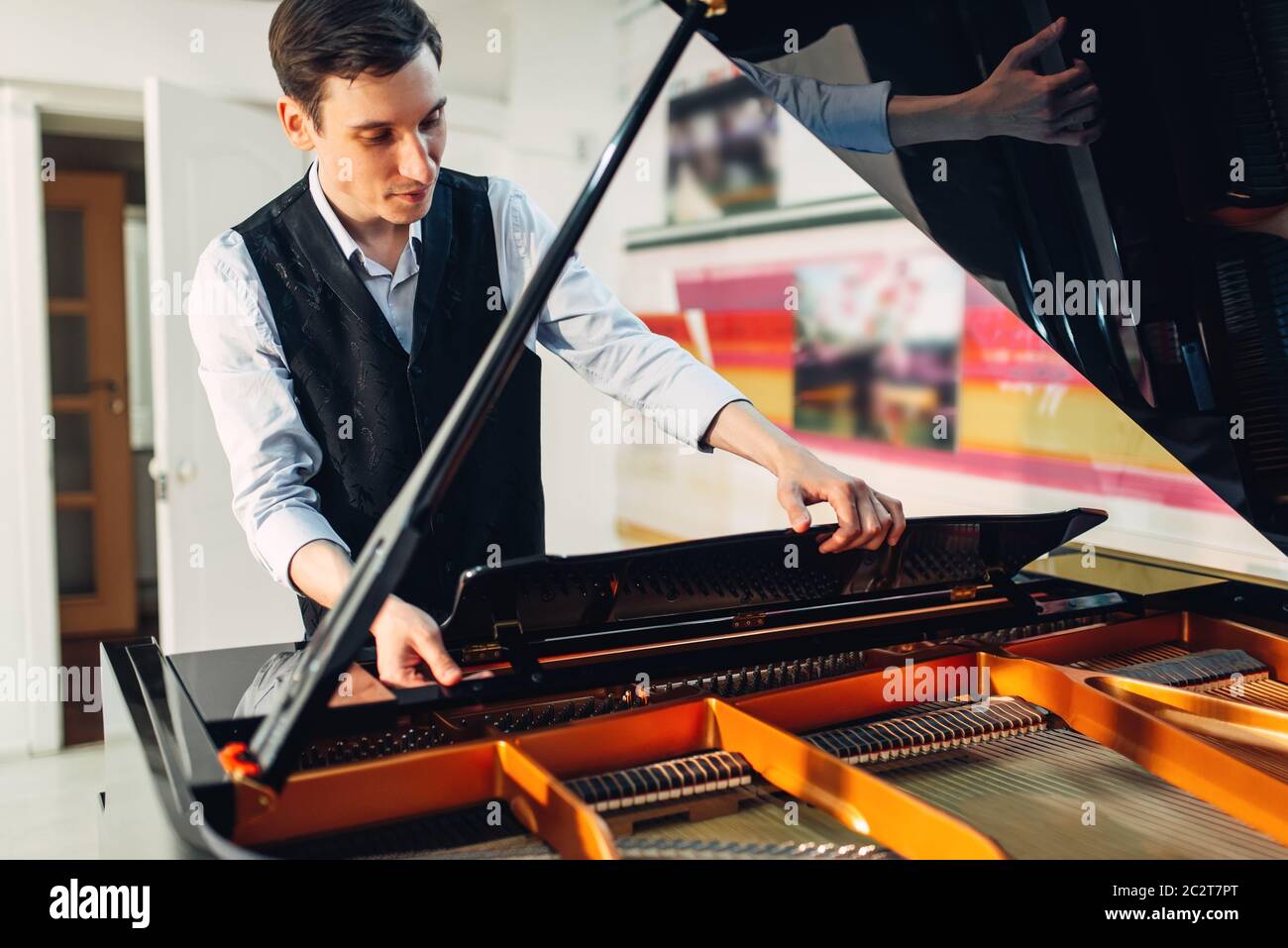Male pianist opens the lid of the black grand piano. Musician adjusts ...