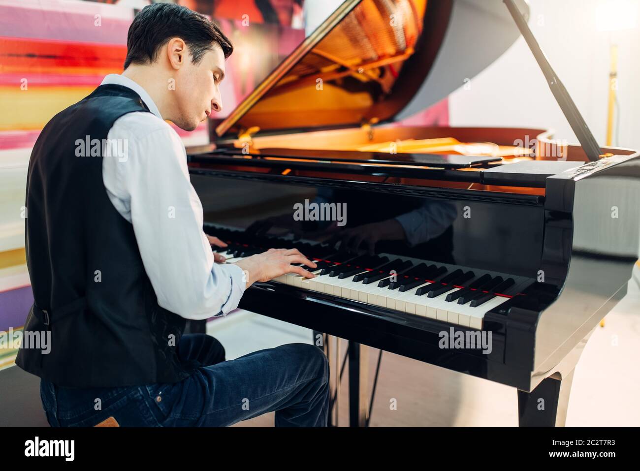 Male pianist at the classical black grand piano, performance in studio ...