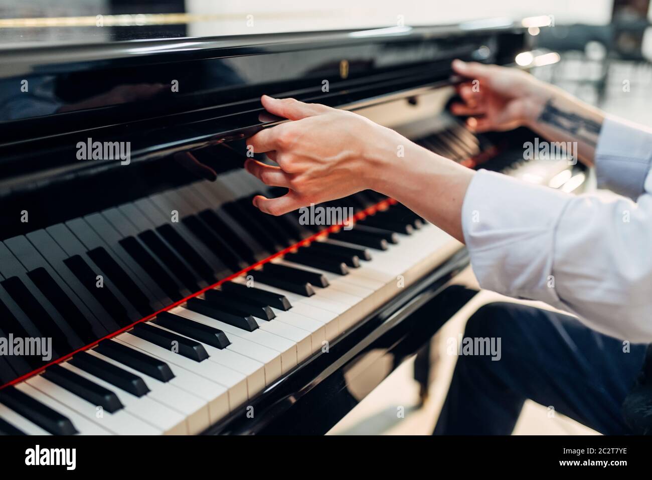 Male pianist opens the keyboard lid of the black grand piano. Musician ...