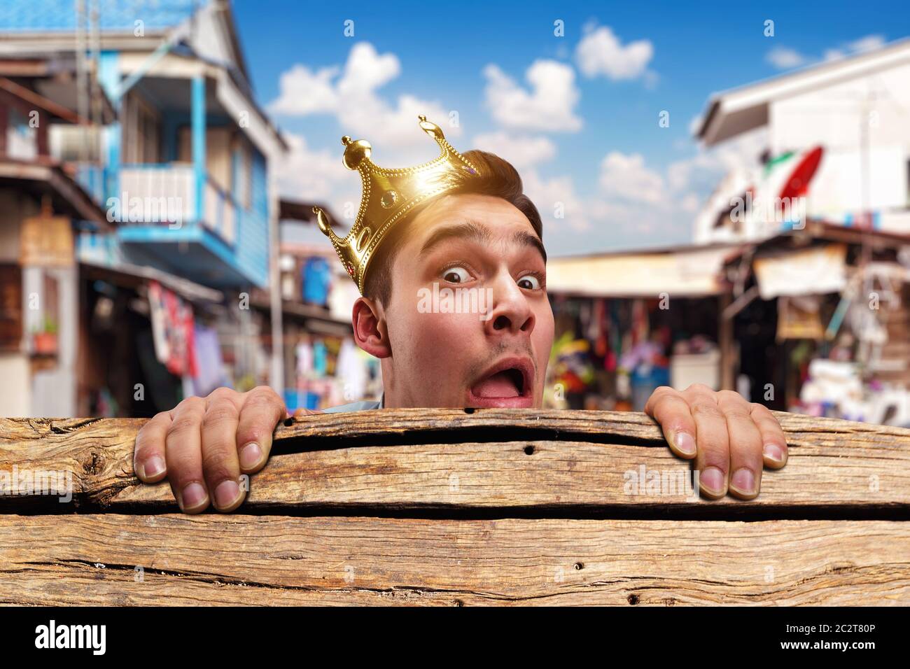 Scared pauper man with crown on the head hidding behind the wooden ...