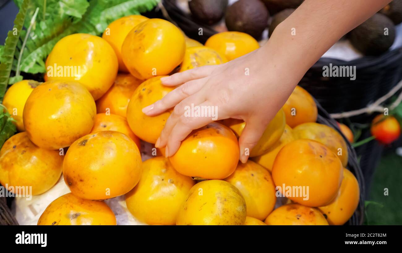 Woman's hand picks persimmons in a store Stock Photo - Alamy