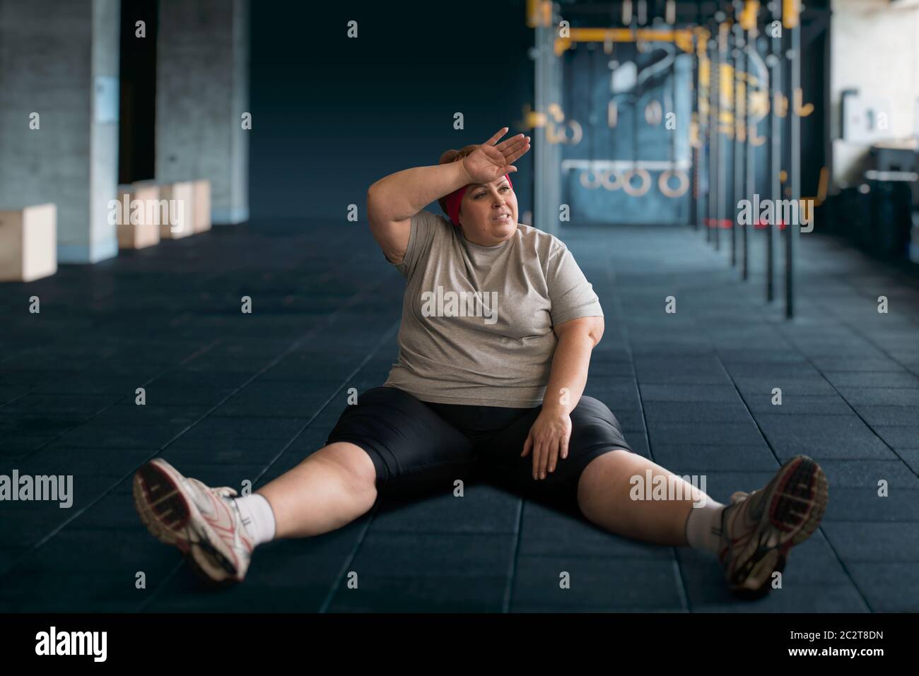 Tired overweight woman sits on the floor in gym. Calories burning ...