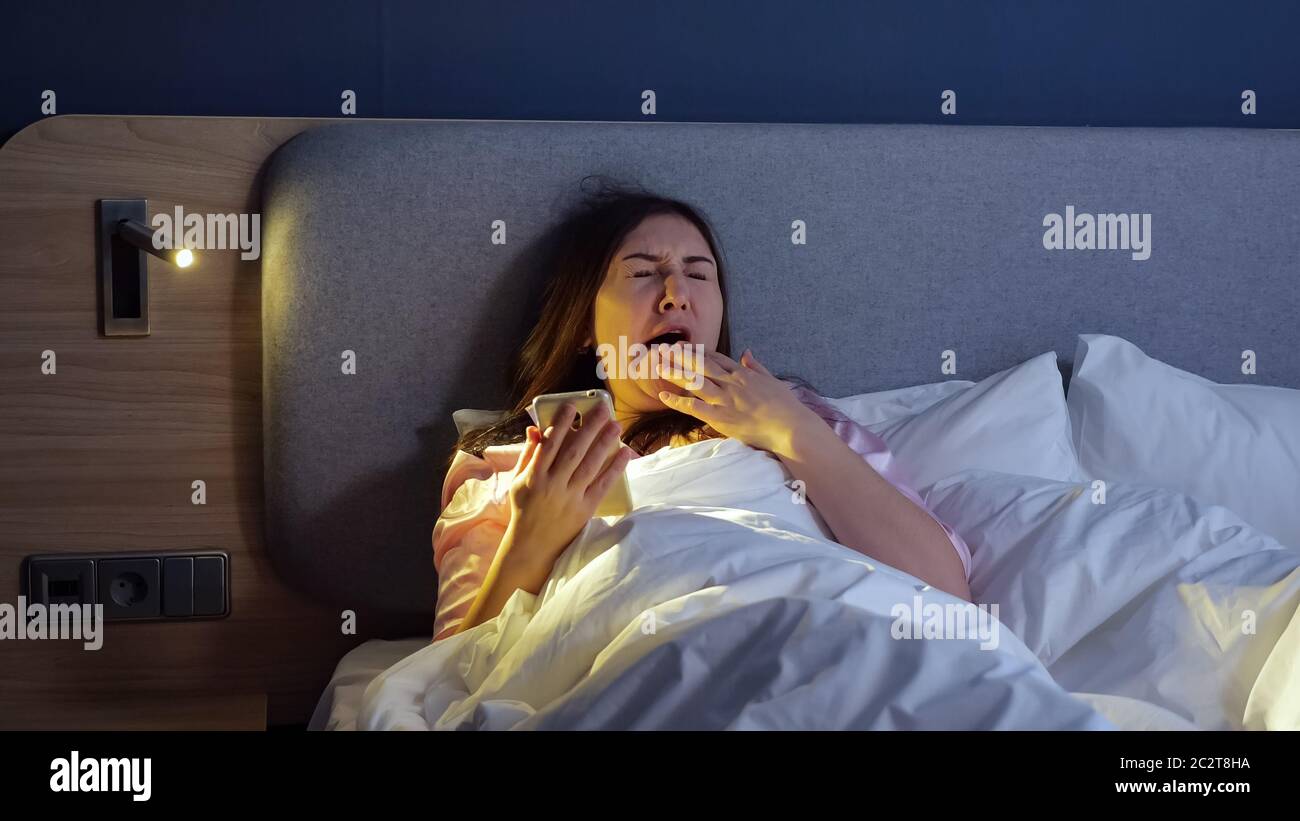 beautiful tired lady in pink pajama surfs internet with phone before ...