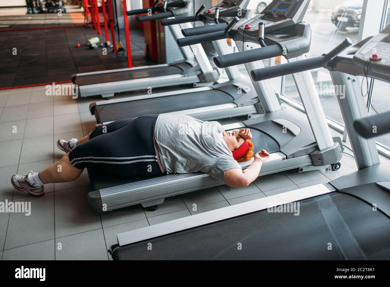 Overweight tired woman lies on a treadmill after running in gym ...