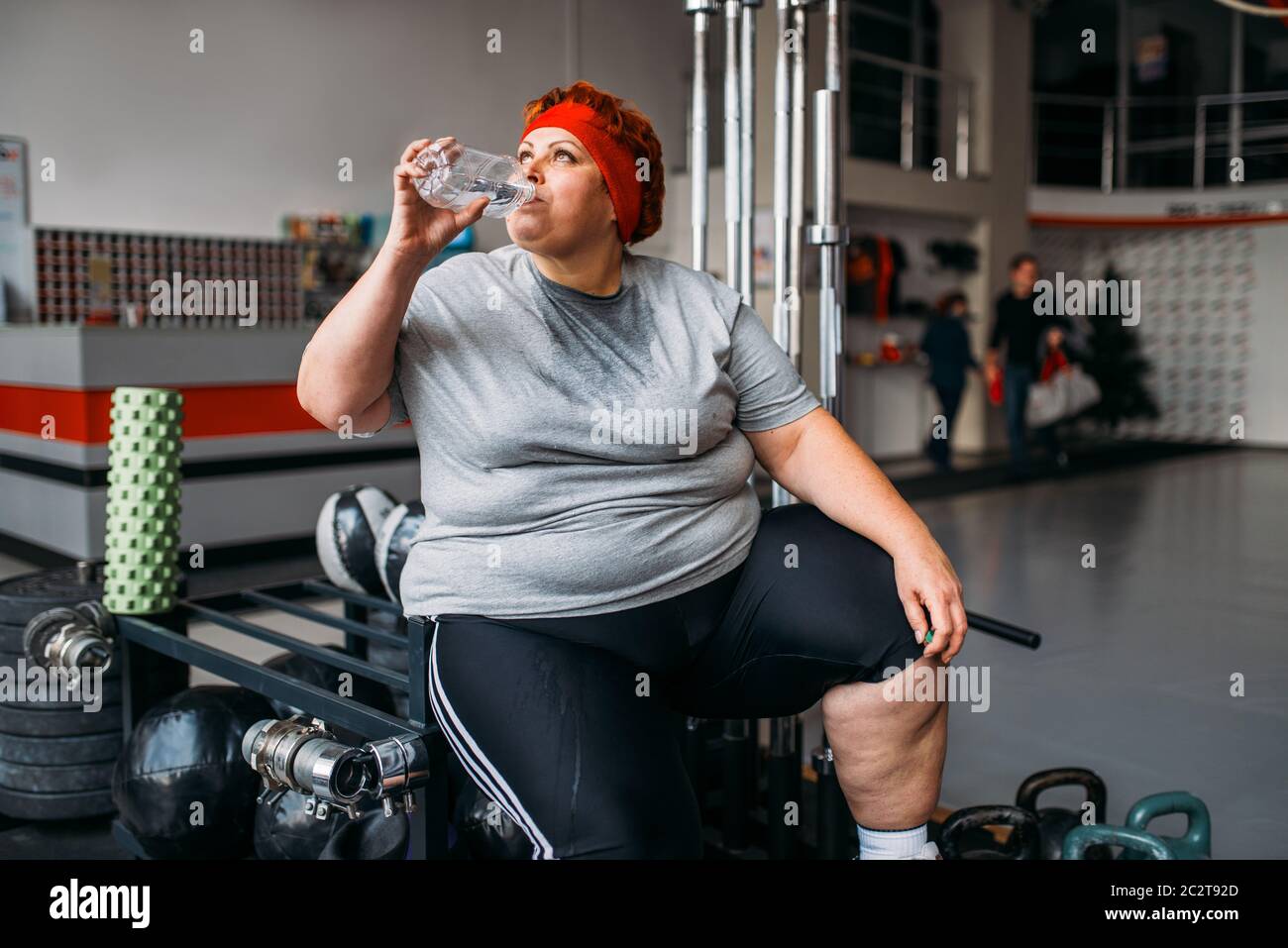 Fat sweaty woman drinks water after active training in gym. Calories ...