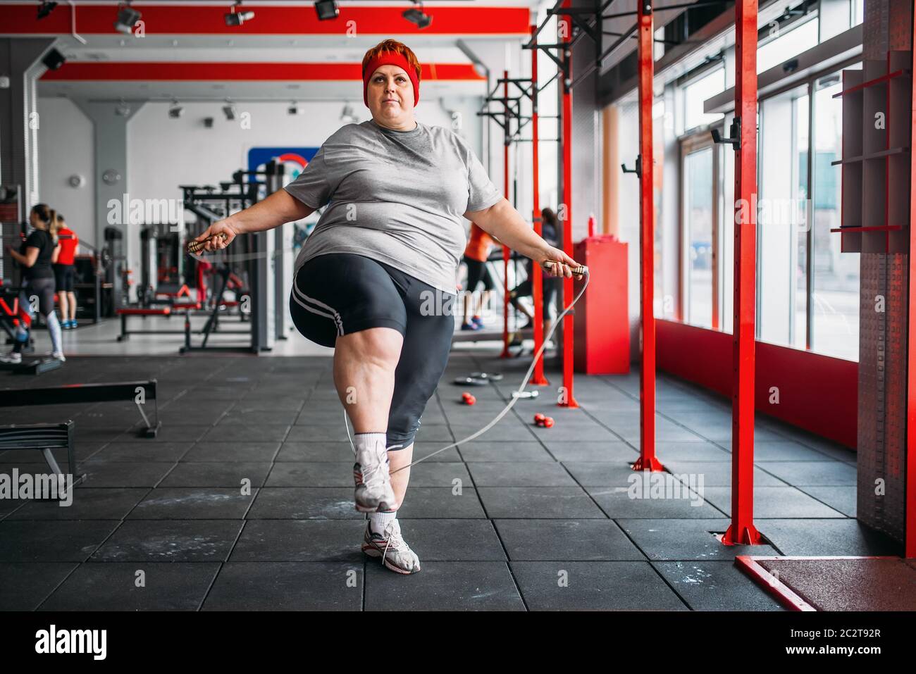 Fat sweaty woman doing exercise with rope in gym. Calories burning ...