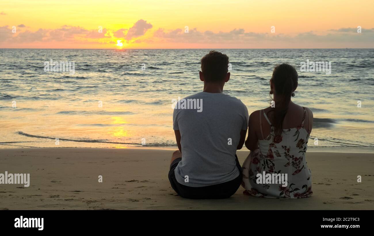 silhouette of lovely young couple sits on empty ocean beach watching ...