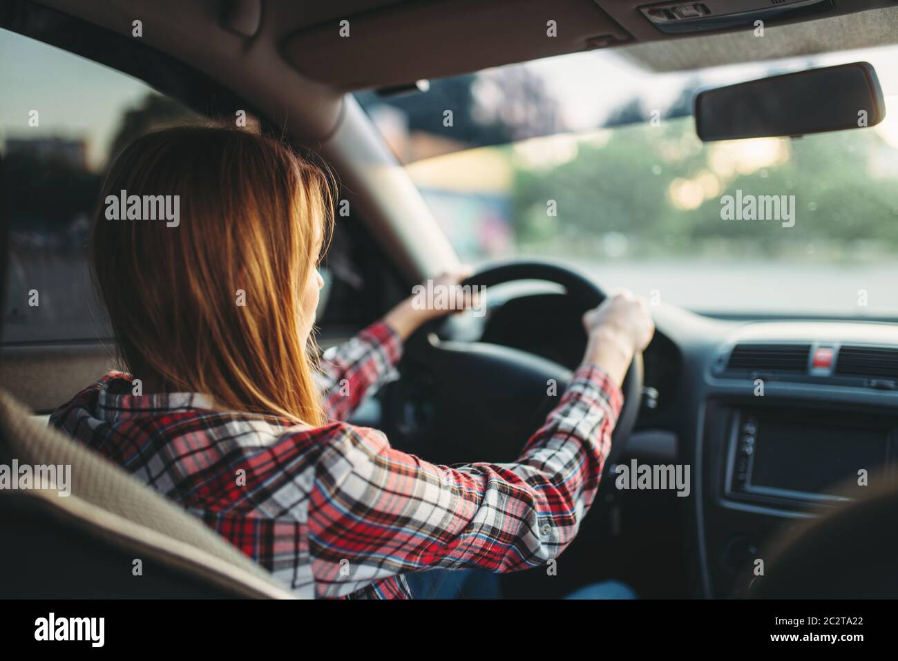 Young woman beginner driving a car, back view. Female person in vehicle ...