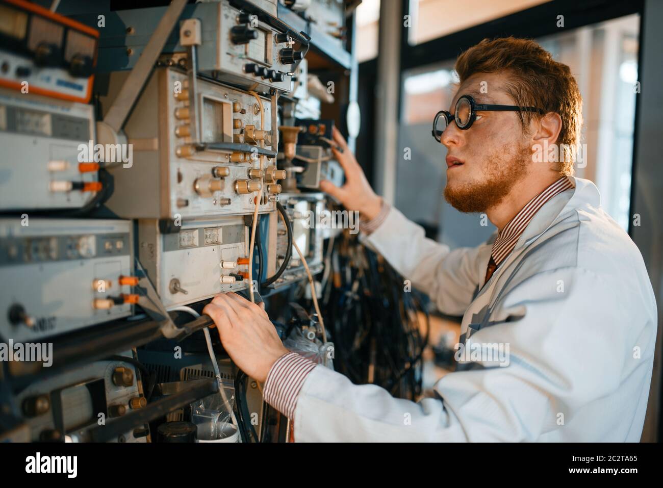 Crazy scientist in glasses adjusts electrical device in laboratory ...