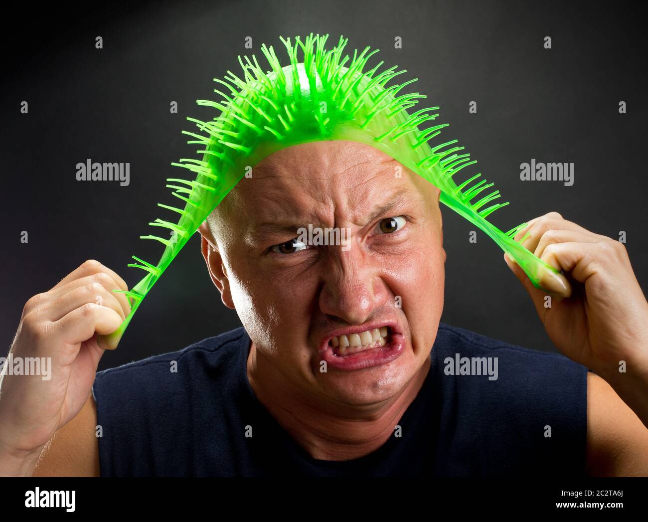 Mad man pulling on spiky green rubber hat Stock Photo - Alamy