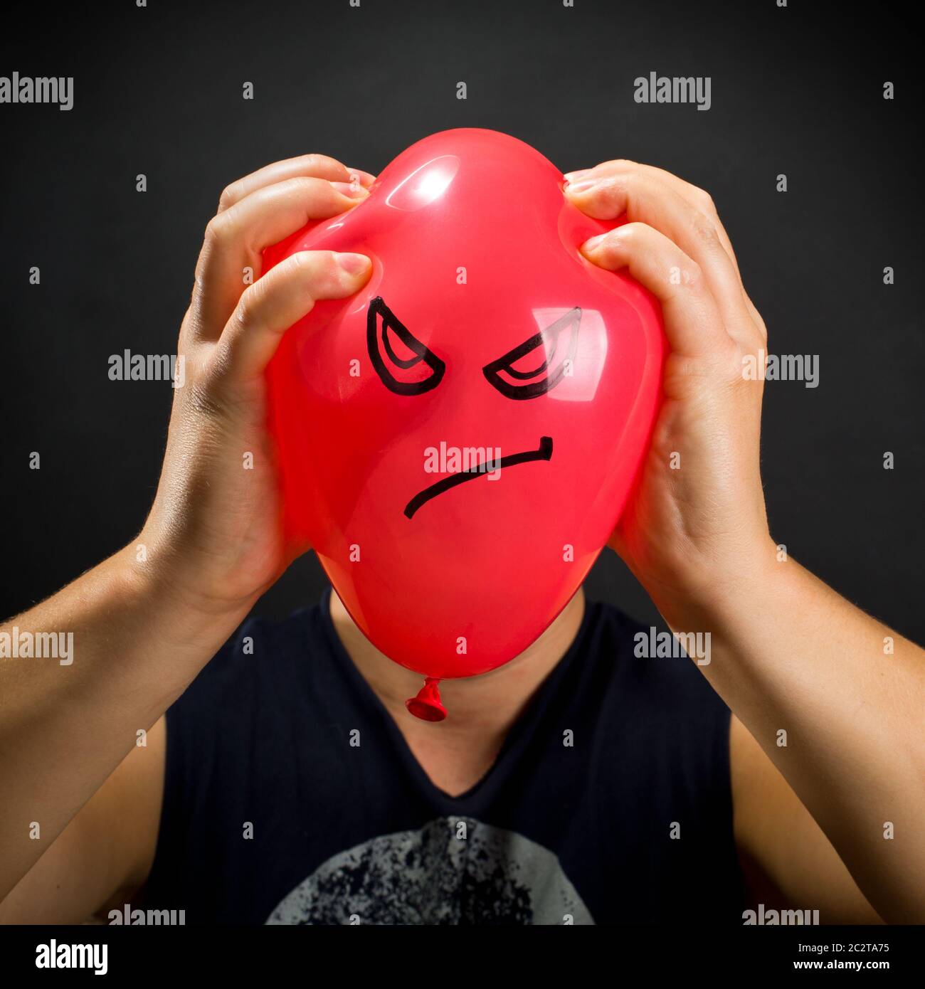 Man squeezing red balloon with angry smiley Stock Photo - Alamy