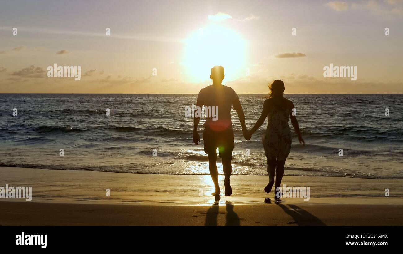 young couple run joining hands on beach to ocean against sunset closeup ...