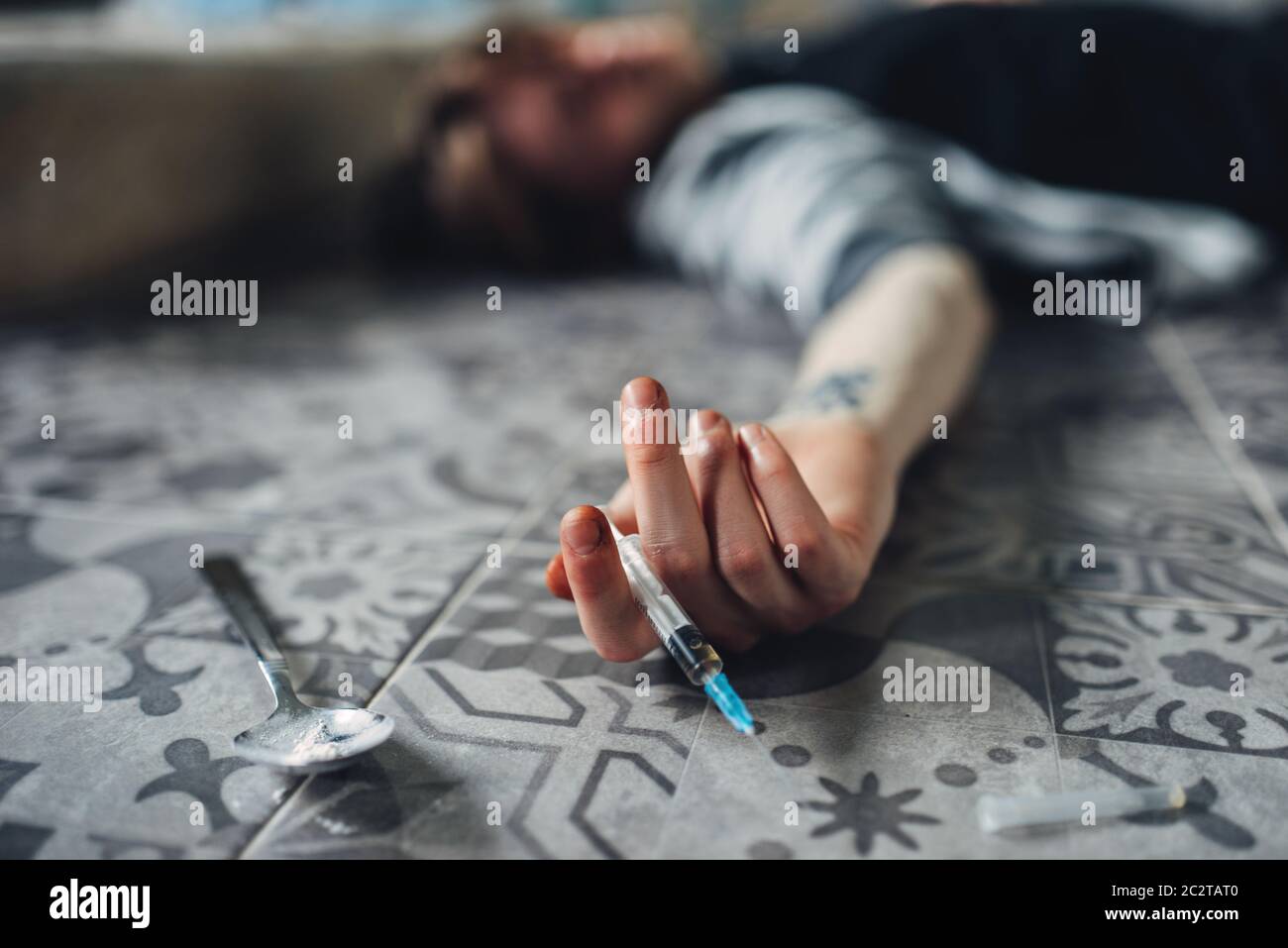 Drug addict lies on the floor, hand with syringe and spoon for dose ...