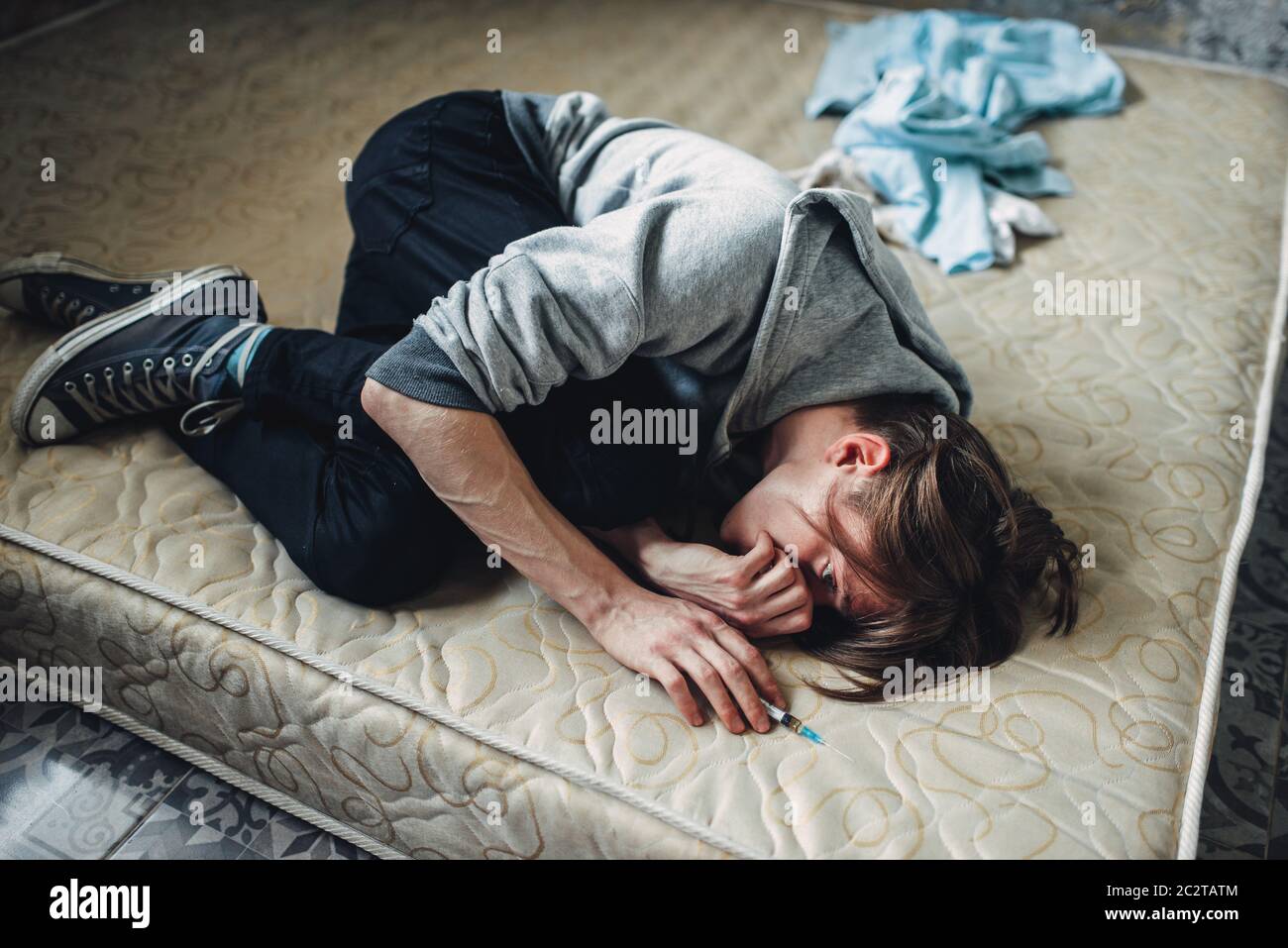 Male drug addict with syringe in hand sleeping in bed after dose ...