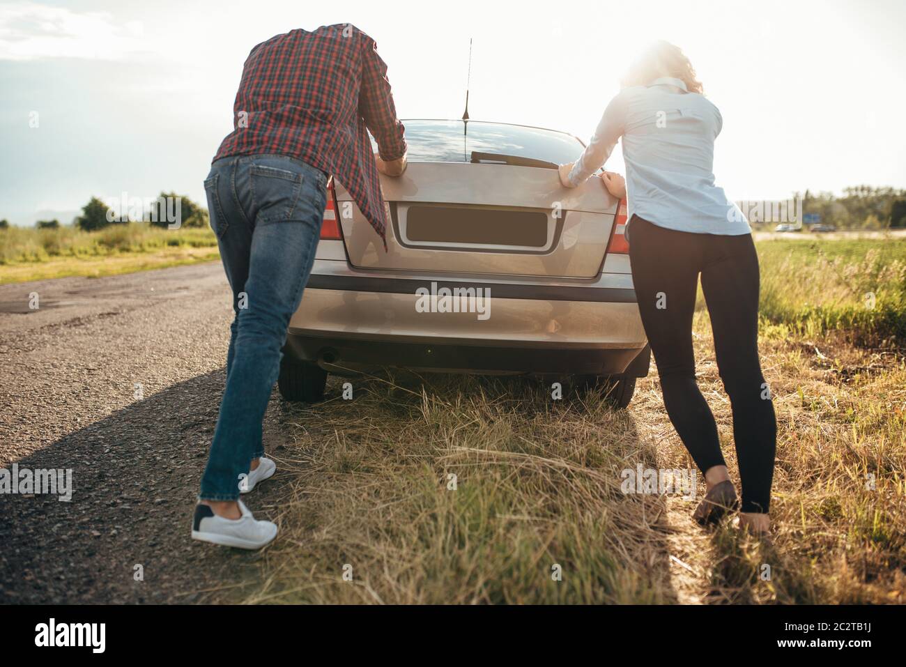 Man and woman pushing a broken car down the road, back view. Vehicle ...