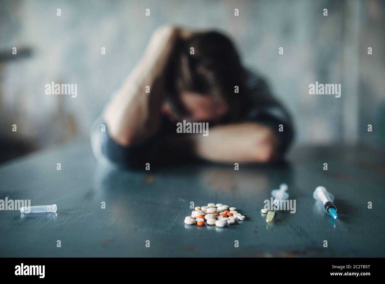 Male junkie sitting at the table with drugs and syringe, grunge room ...
