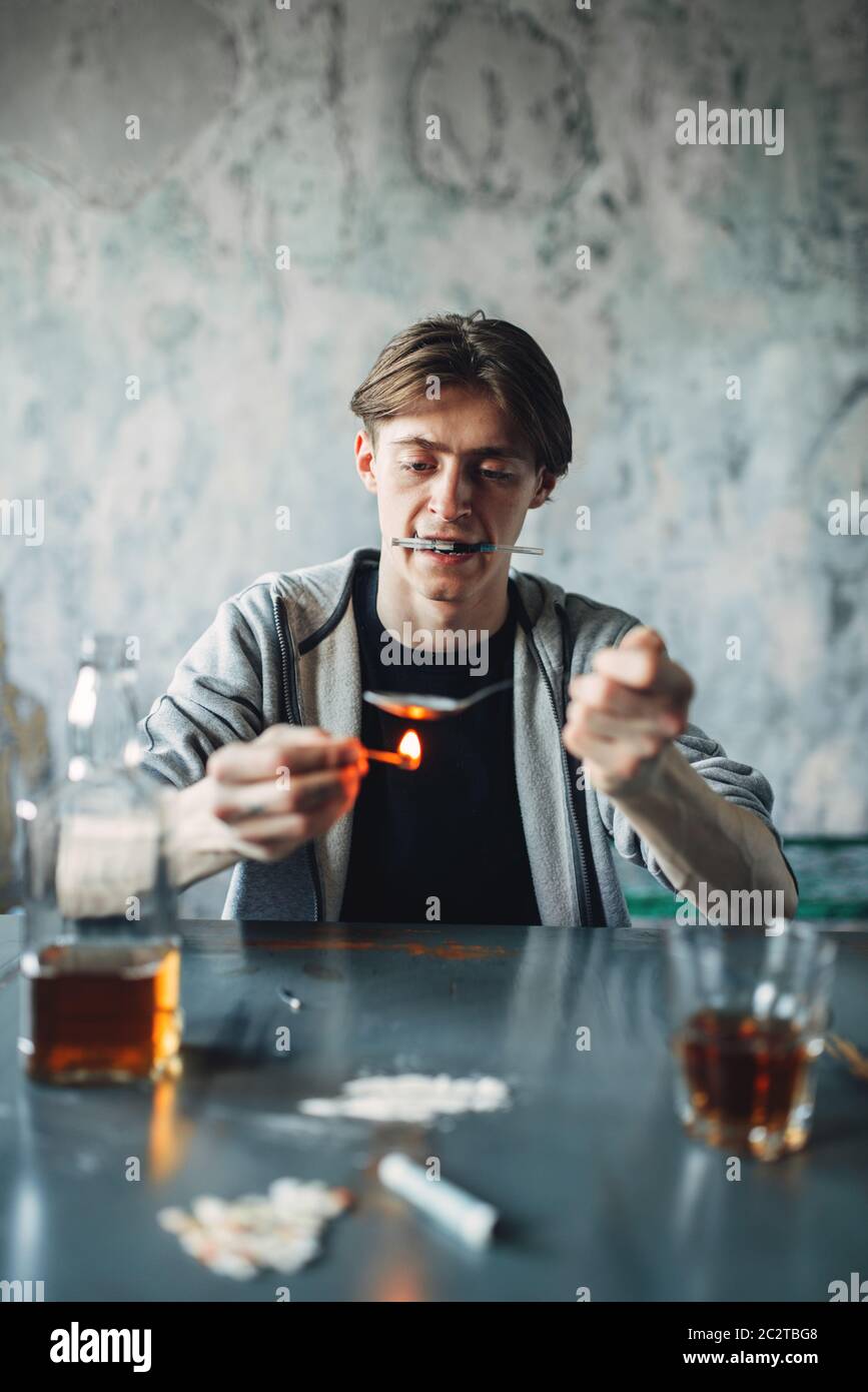 Drug addict with a spoon and matches prepares a dose. Narcotic ...