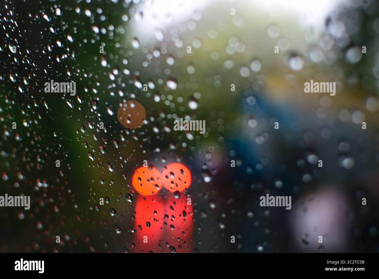 Rain drops on a glass with visible red lights of a car through the ...